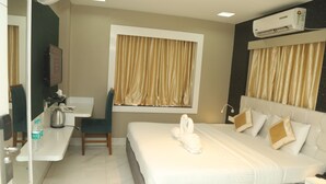 Quarto de hotel com cama, mesa de cabeceira, cadeira e aparelho de ar condicionado.
