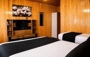 Quarto de hotel com parede revestida em madeira, TV de tela plana fixada em uma prateleira de madeira, cama com roupa de cama preta e branca e uma grande obra de arte floral acima da TV.