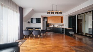 Cozinha moderna com armários de madeira, forno embutido e bancada preta. Há uma área de jantar com mesa redonda e cadeiras pretas.