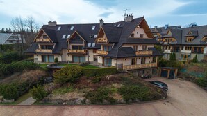Uma casa grande e de vários andares com telhado inclinado, varandas múltiplas e um jardim bem cuidado.