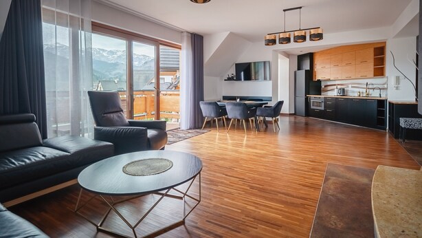 Uma sala de estar moderna com um sofá, uma mesa de centro redonda e uma área de jantar com cadeiras.