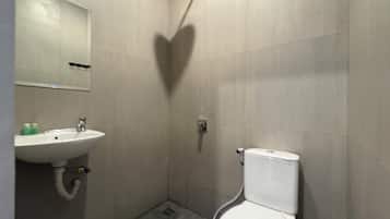 Um banheiro pequeno com pia, vaso sanitário e chuveiro, todos brancos.