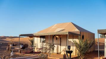 Acampamento no deserto com uma única tenda, área de estar externa e um pequeno jardim.
