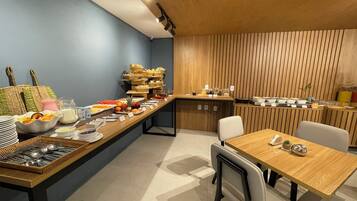 Buffet de café da manhã com diversos alimentos e área de estar com cadeiras e mesa.