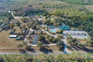 Vista aérea de um empreendimento com vários edifícios, uma piscina e uma estrutura grande com telhado verde.