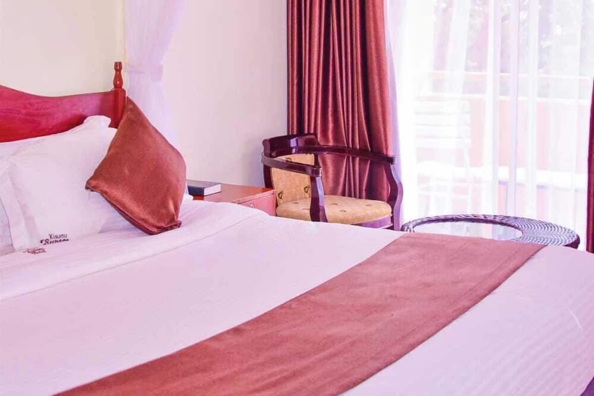 Quarto de hotel com cama, cadeira, mesa de cabeceira e janela com cortinas.