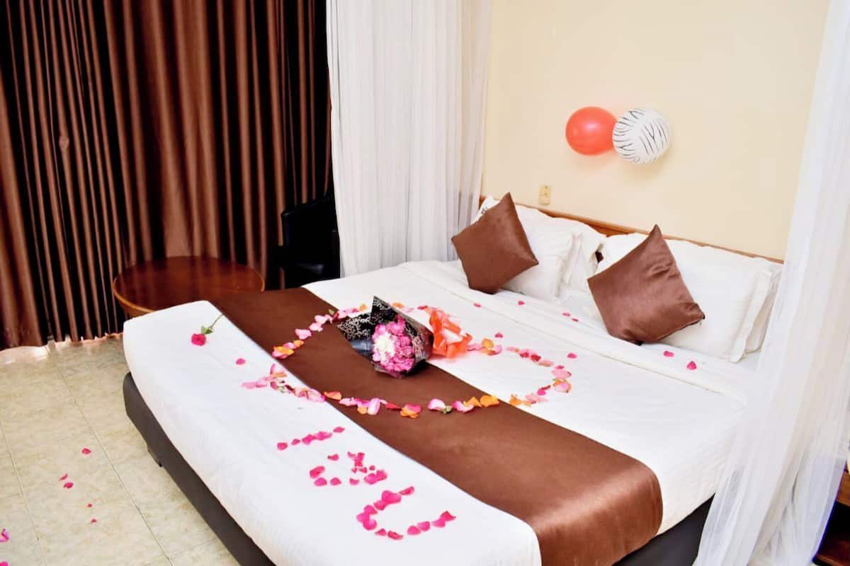 Uma cama bem arrumada com um cobreleite branco e marrom, um buquê de flores e pétalas de rosa dispostas sobre a cama.