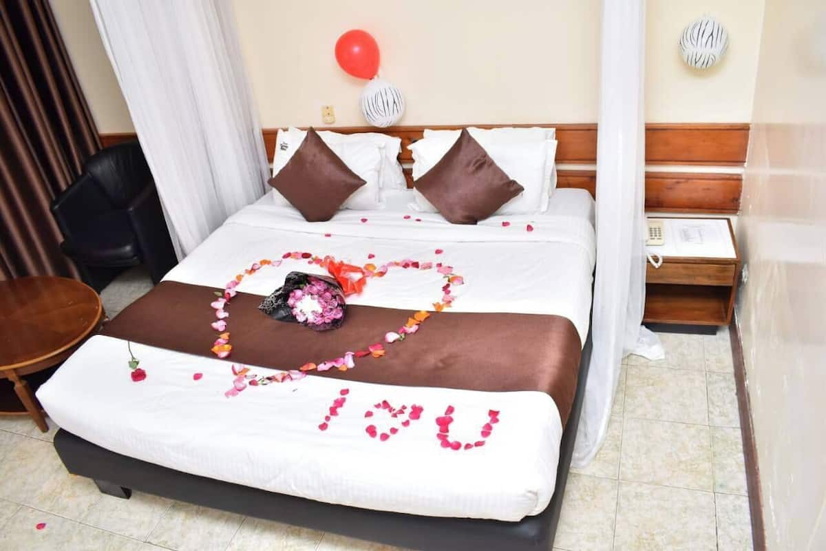 Cama bem arrumada com pétalas de rosa e um arranjo em formato de coração que escreve "I love you" no lençol.