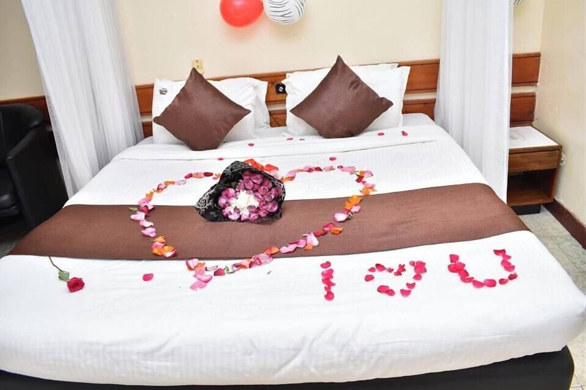 Cama bem arrumada com um arranjo de pétalas de rosa em formato de coração e um pequeno buquê de flores no centro.