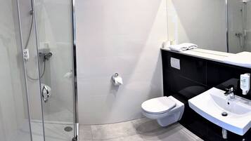 Casa de banho moderna com cabine de duche de vidro, sanita branca e lavatório branco com bancada preta.