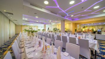 Uma sala de banquetes com fileiras de mesas montadas para um evento formal, com toalhas brancas, talheres e copos.