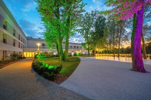 Um pátio com caminho pavimentado, árvores e um edifício com várias janelas e varandas.