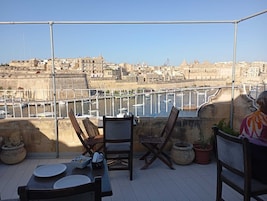 Terraço com mesa e cadeiras, com vista para um porto com barcos e edifícios.