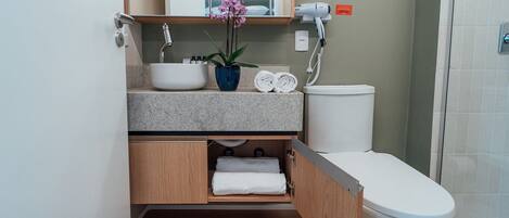 Casa de banho moderna com lavatório branco, um vaso azul com flores, porta-toalhas e sanita.