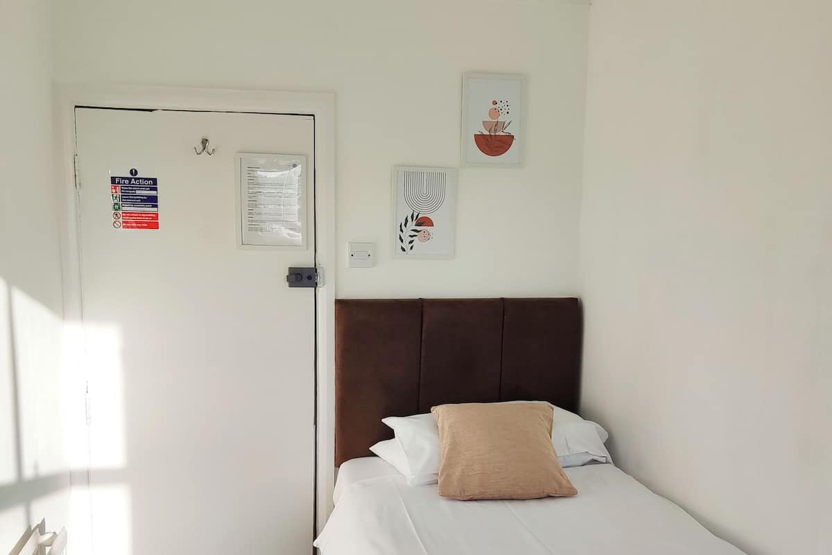 Quarto de hotel com cama, porta com sinal de emergência e parede com quadros emoldurados.