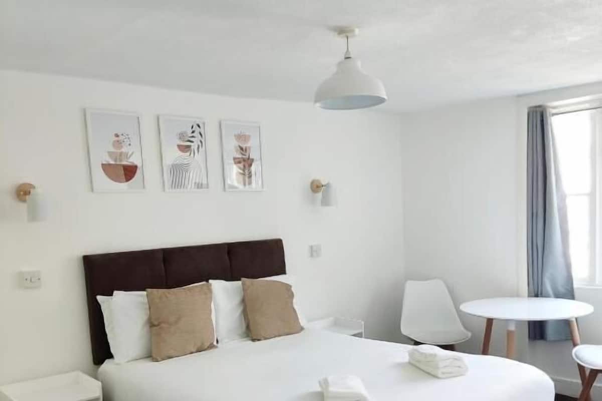 Quarto de hotel bem arrumado com uma cama grande, mesas de cabeceira, uma mesinha redonda e obras de arte na parede.