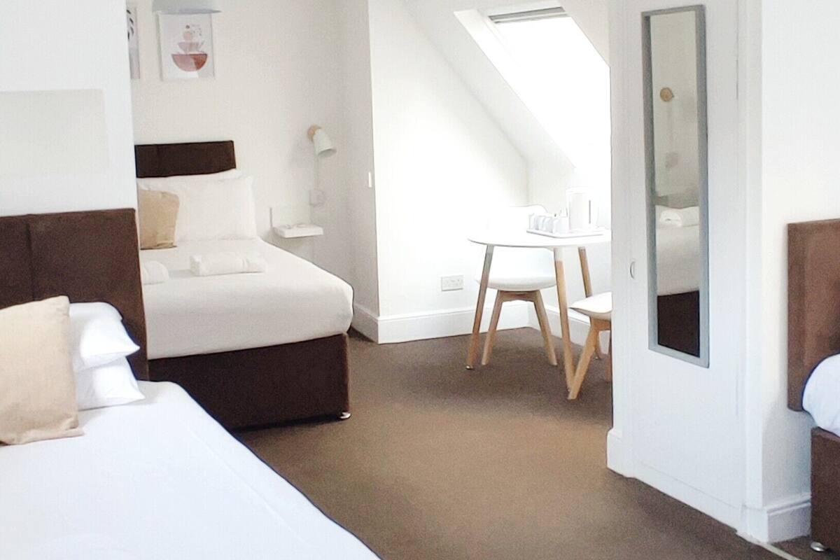 Quarto de hotel com cama, escrivaninha, cadeira, espelho e luminária pendente.
