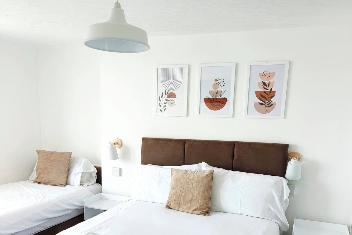 Quarto de hotel com uma cama grande, duas mesas de cabeceira e uma luminária no teto.