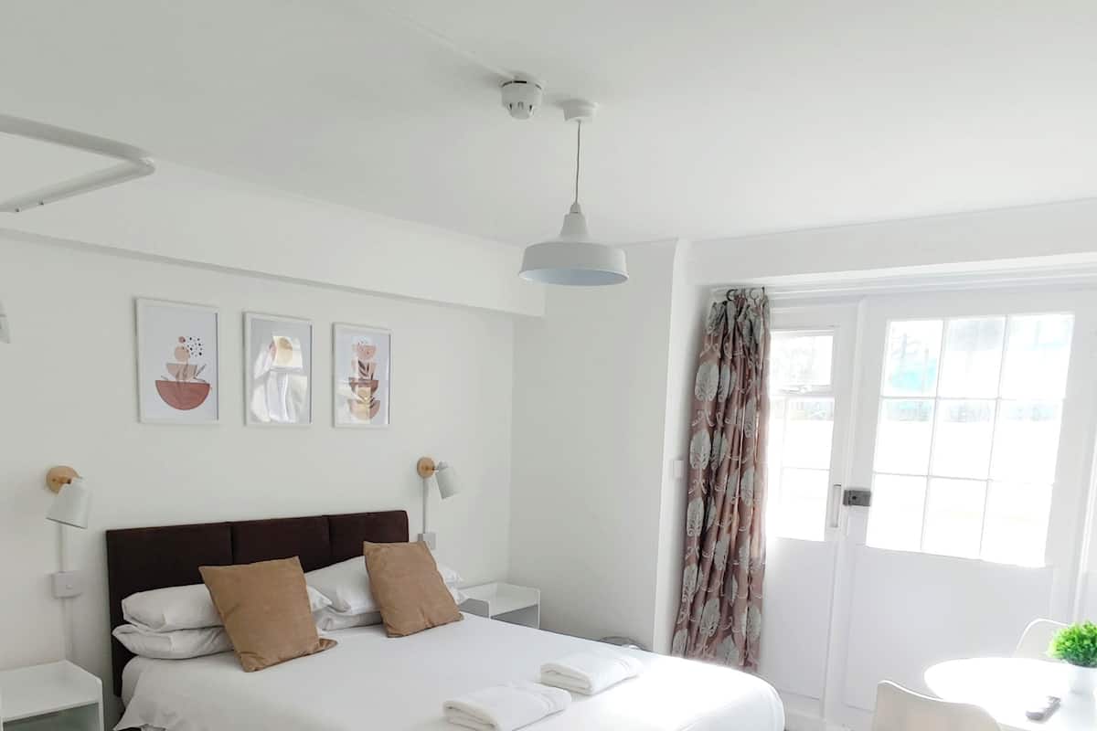 Quarto de hotel com cama, mesas de cabeceira, escrivaninha, cadeira e janela com cortinas.