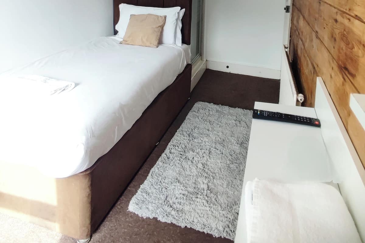 Quarto com uma cama, luminária de teto branca, parede de madeira e um tapete pequeno.