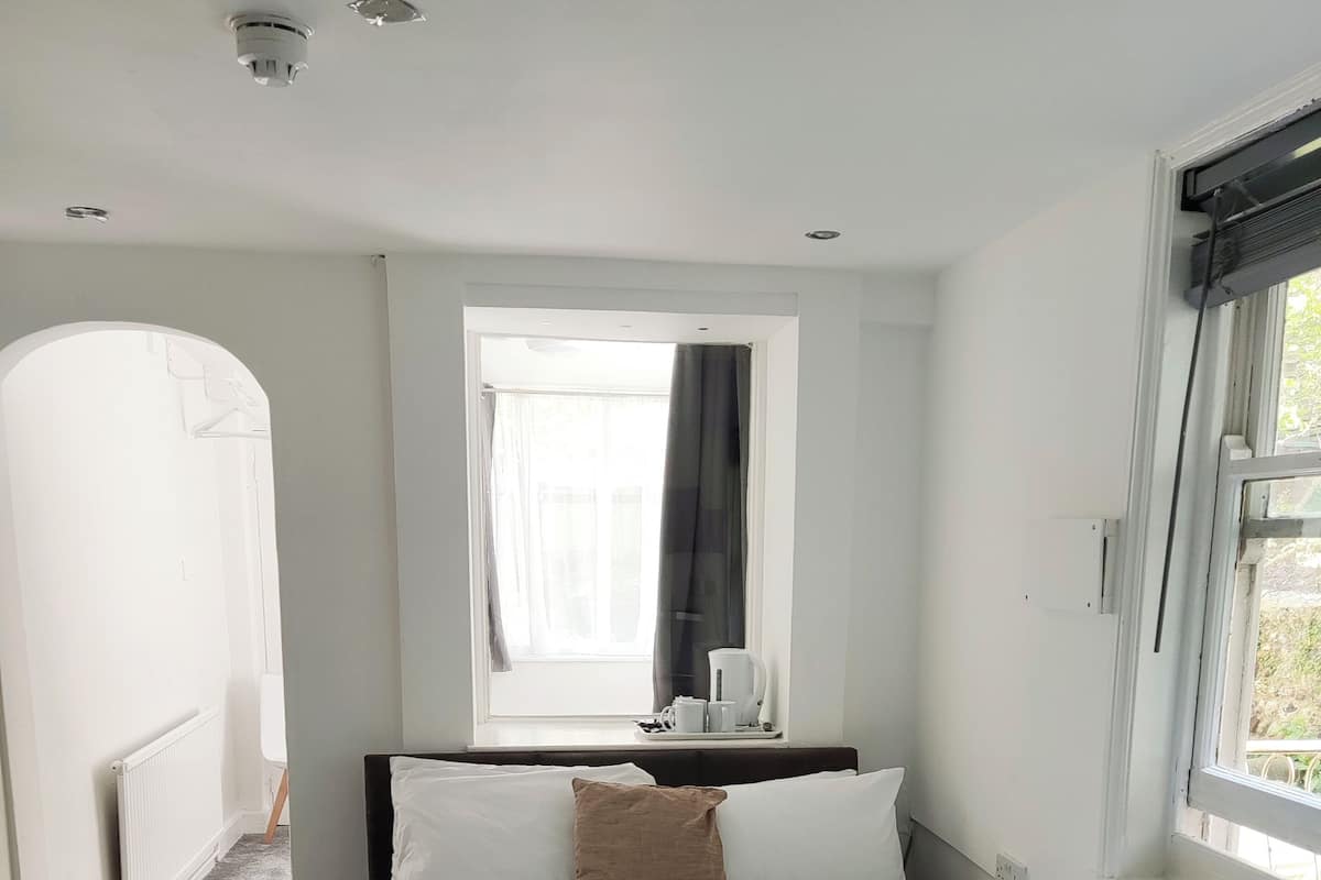 Quarto de hotel com uma cama grande, uma janela com cortinas, uma mesa de cabeceira com abajur e um radiador.