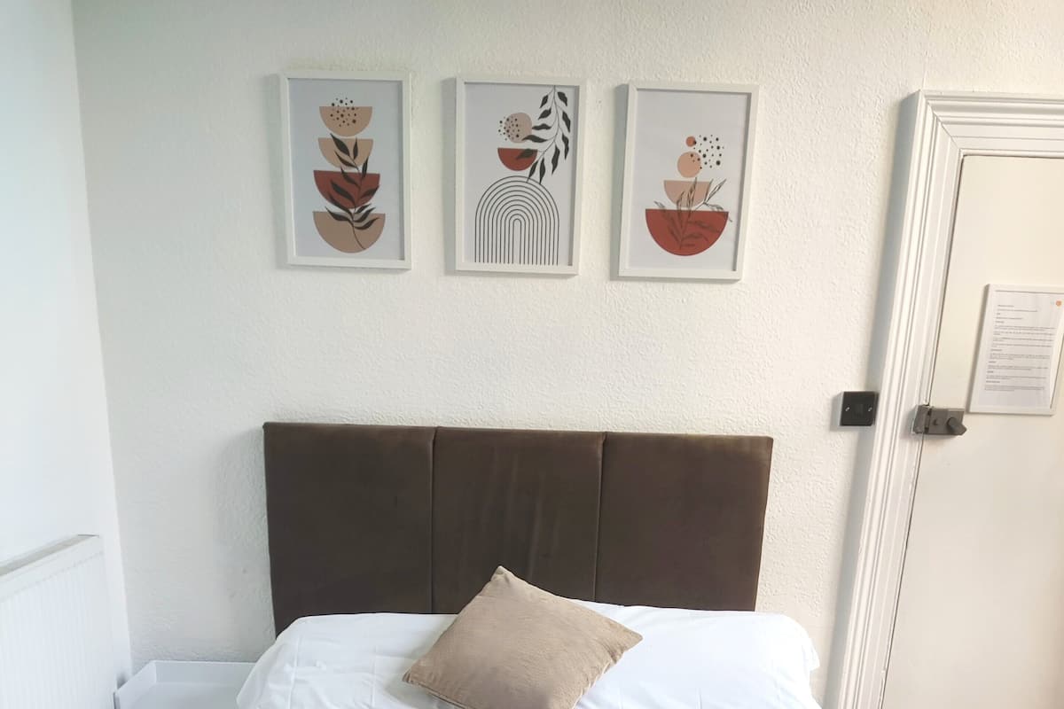 Uma cama bem arrumada com duas toalhas, um travesseiro marrom e três obras de arte emolduradas na parede.