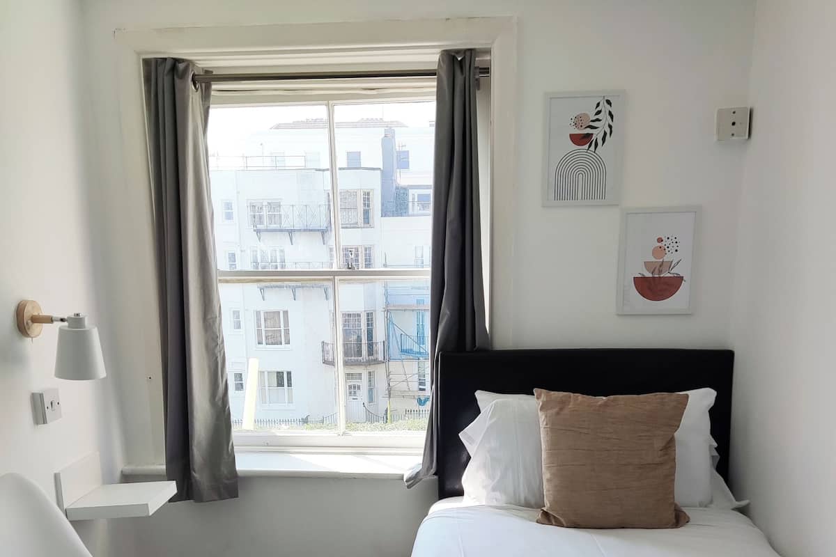 Quarto de hotel com cama, uma cadeira, janela com cortinas e obras de arte na parede.