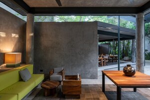Um interior moderno com sofá verde, cadeiras de madeira, uma mesa e uma janela grande com vista para um jardim.