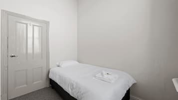 Uma cama de solteiro num quarto com paredes brancas e porta fechada.