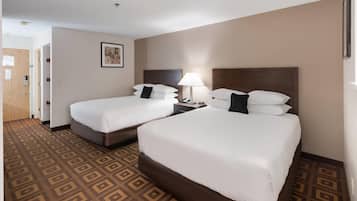 Quarto de hotel com duas camas, uma mesa de cabeceira com abajur e um tapete estampado.