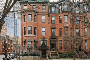 Fileira de edifícios em estilo brownstone, com várias janelas e uma entrada central.