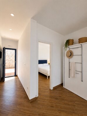 Quarto de hotel com piso de madeira, uma cama com roupa de cama branca, um porta-toalhas fixado na parede e uma porta que dá para uma varanda.