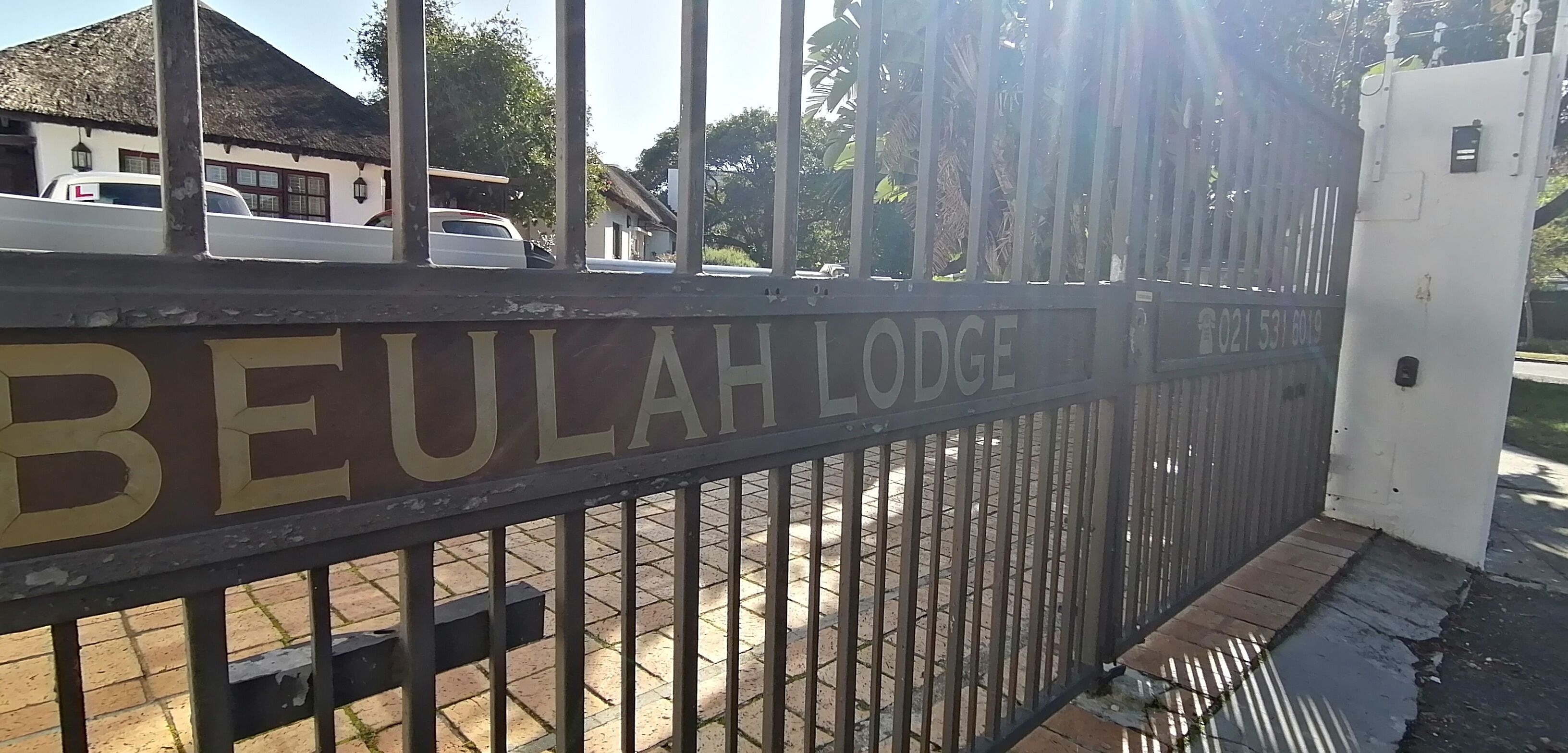 Entrada com portão para Beulah Lodge, com cerca de metal e uma placa.