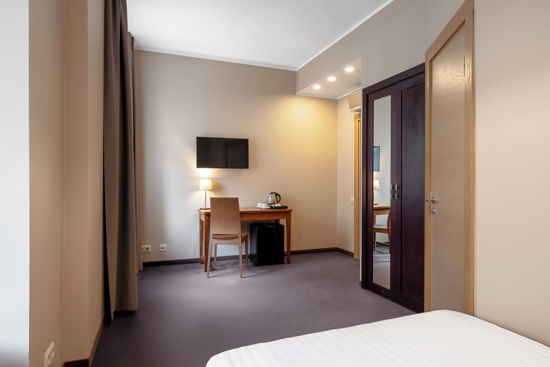 Quarto de hotel com cama, secretária com cadeira, televisão e máquina de café.