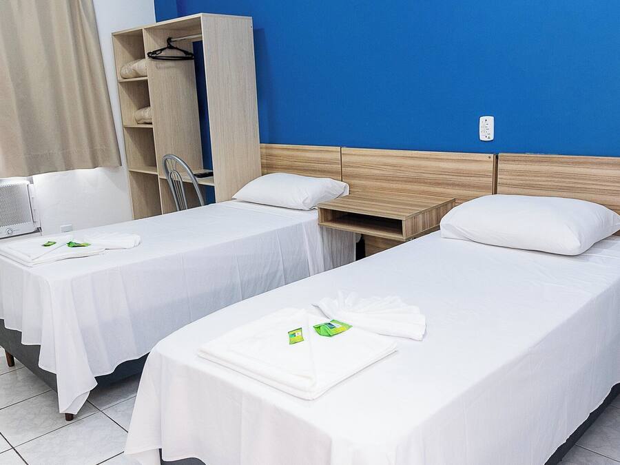 Quarto de hotel com duas camas individuais, um guarda-roupa, um aquecedor e parede azul.