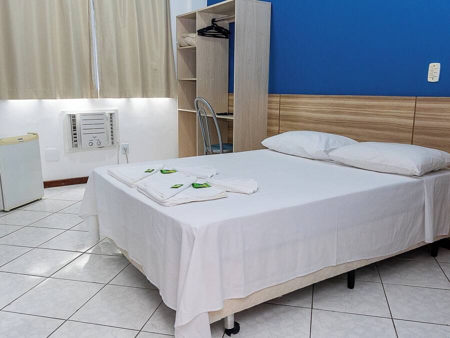 Cama bem arrumada com lençóis brancos, cabeceira de madeira e parede azul.