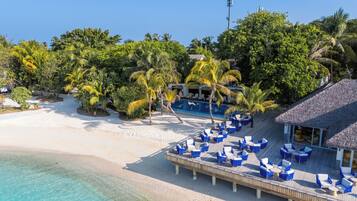 Um resort à beira-mar com piscina, espreguiçadeiras e um edifício com telhado de palha.
