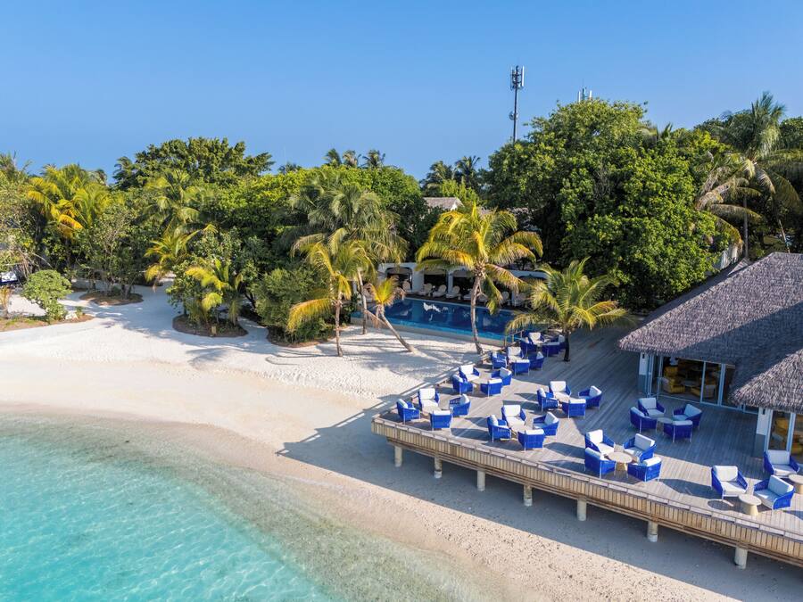 Um resort à beira-mar com piscina, espreguiçadeiras e um edifício com telhado de palha.
