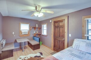 Um quarto com cama, arranhador para gato, porta de madeira e ventilador de teto.