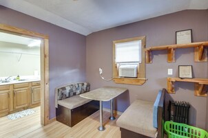 Quarto que aceita animais de estimação com um banco de madeira, uma mesinha, uma casinha verde para animais e uma prateleira fixada na parede.