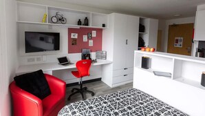Quarto moderno e bem organizado com uma cadeira vermelha, uma escrivaninha com um laptop, uma televisão e diversas estantes com objetos.