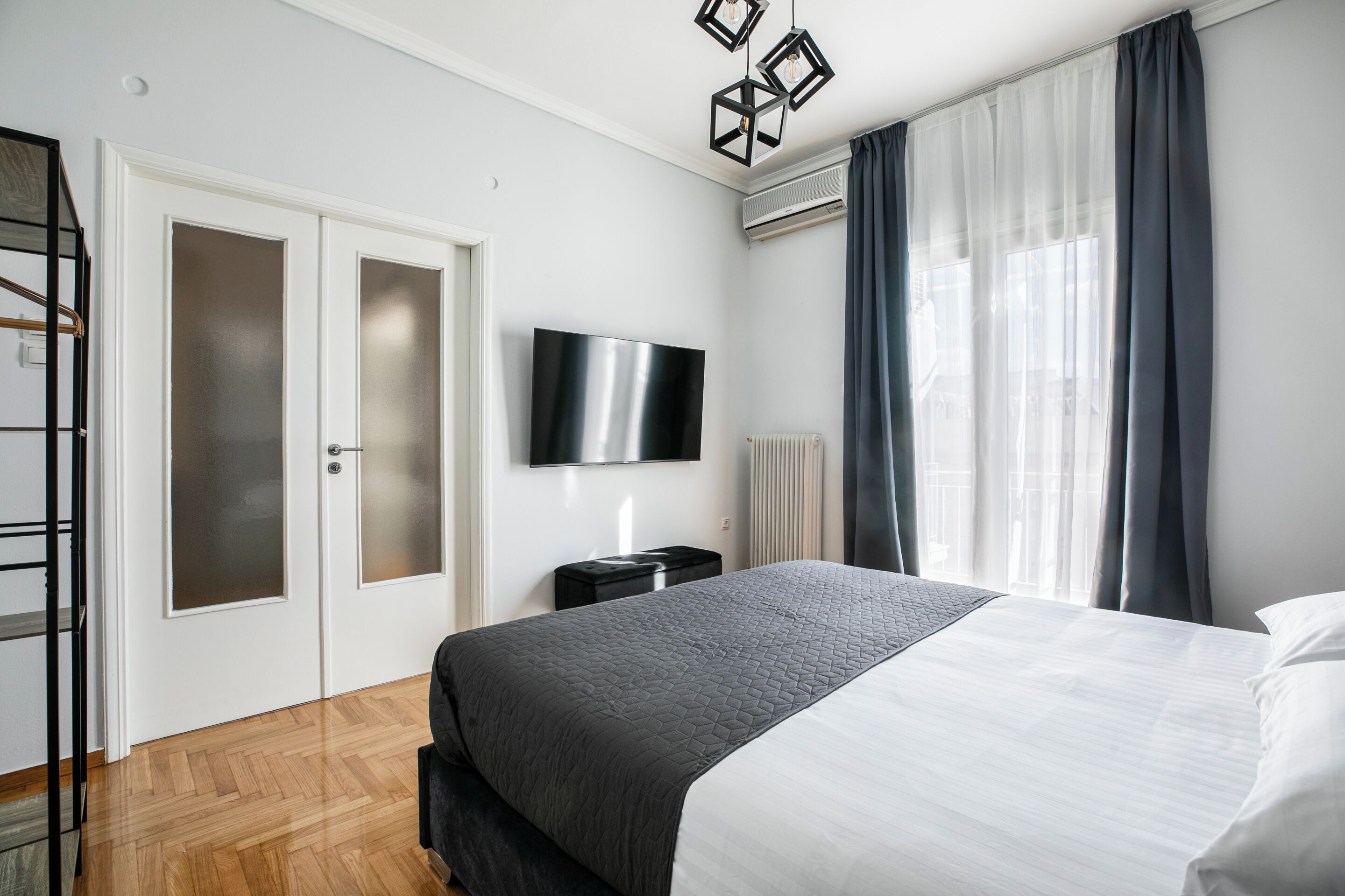 Quarto de hotel moderno com uma cama, televisão, guarda-roupa e janela com cortinas.