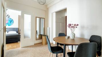 Quarto de hotel moderno com uma mesa de jantar de madeira, quatro cadeiras, um vaso com flores e um espelho grande.