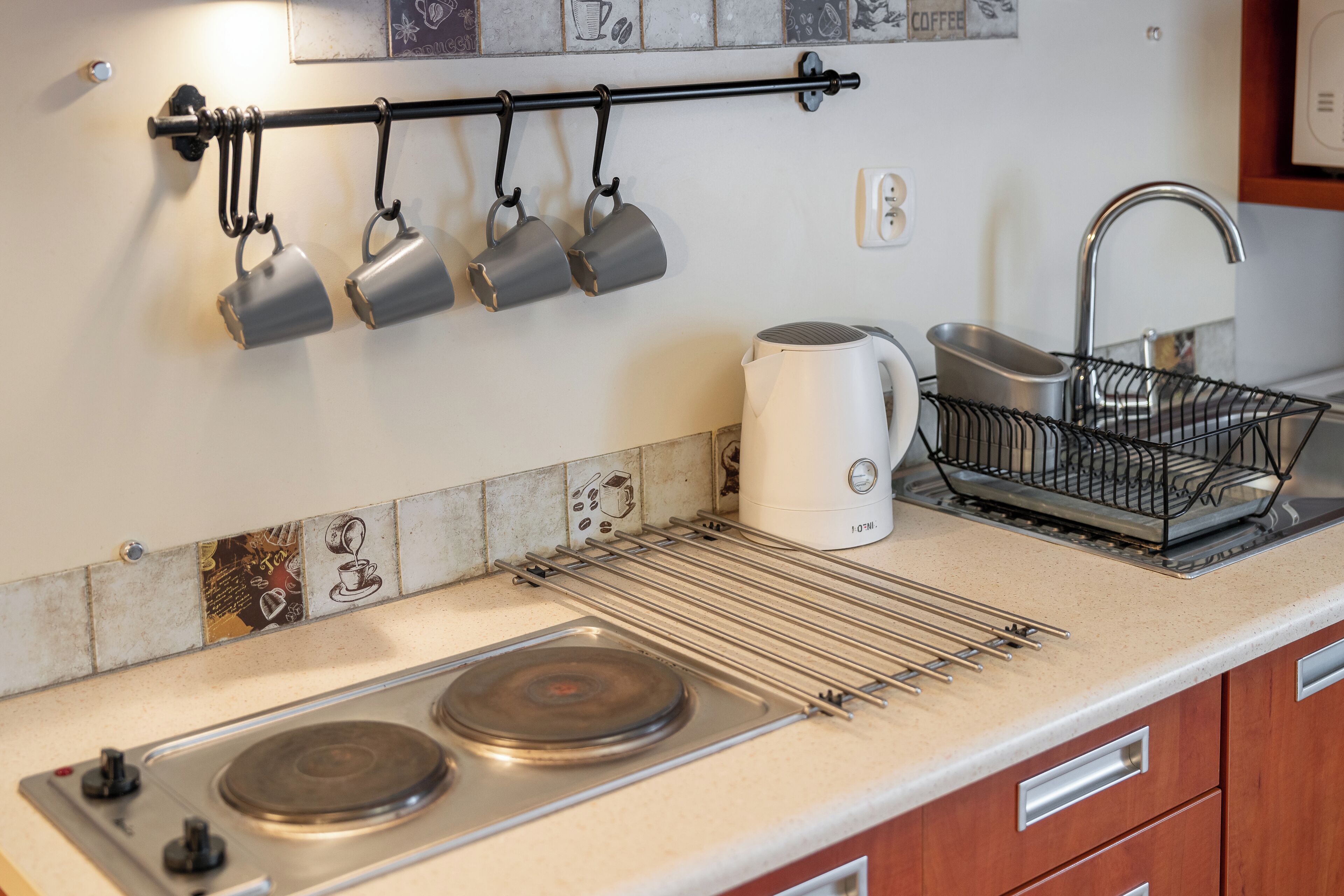 Uma cozinha com fogão, cafeteira e suporte para canecas.
