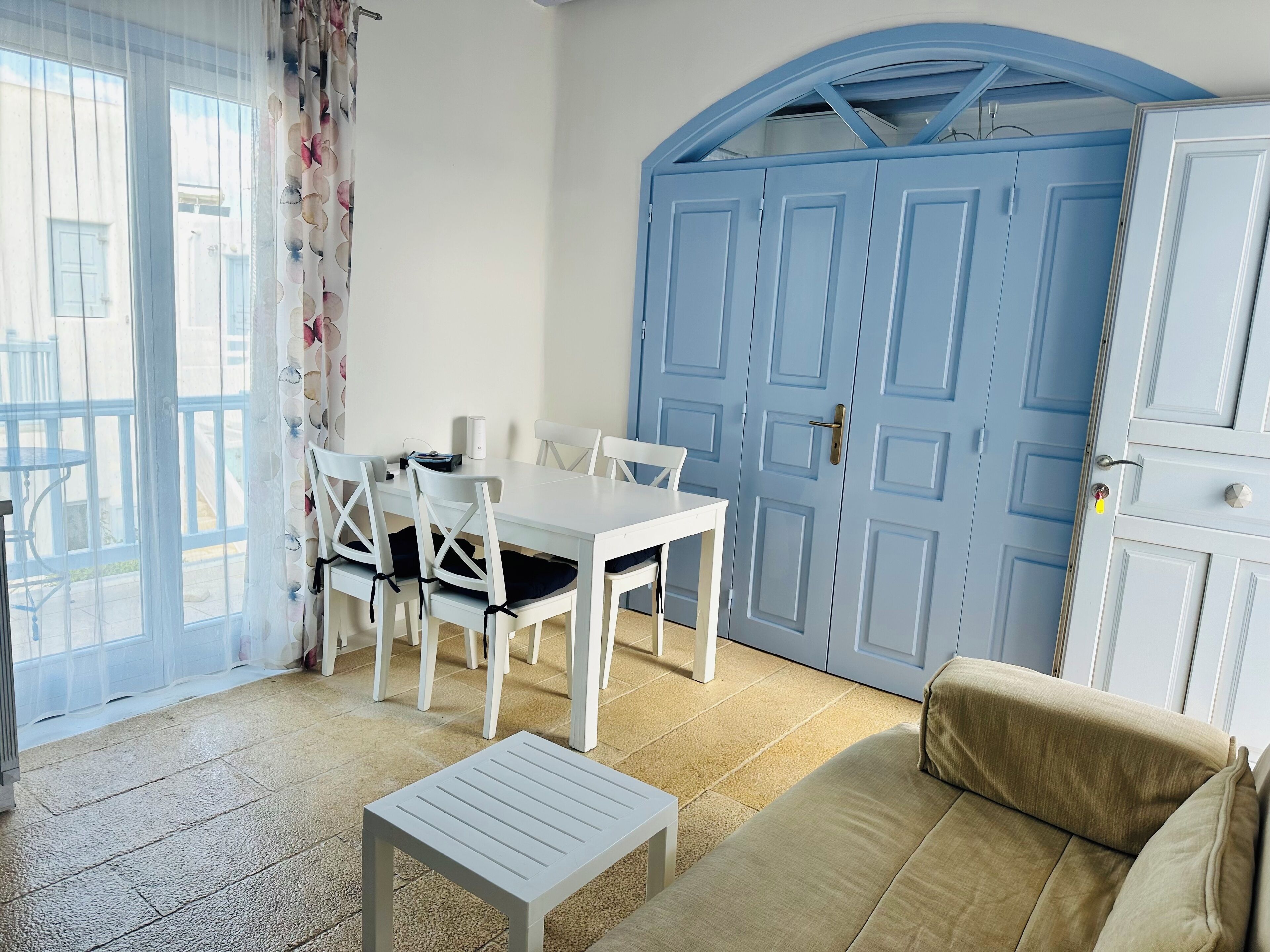 Quarto com mesa de jantar, cadeiras, sofá e porta arqueada azul.