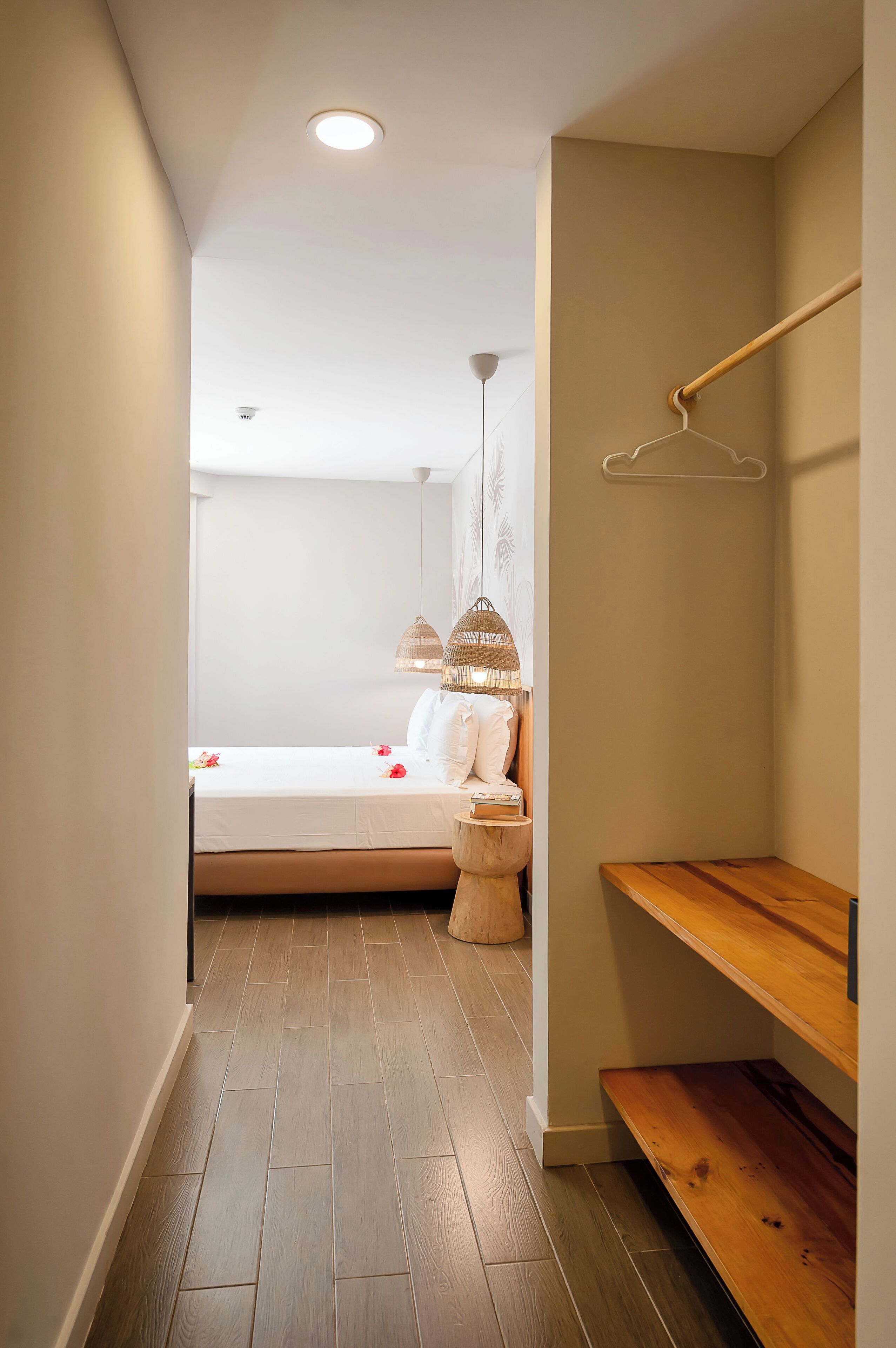 Um corredor estreito que leva a um quarto com cama, mesa de cabeceira e luminária pendente.