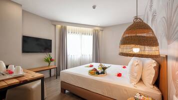 Quarto de hotel com cama, mesa de cabeceira, televisão e área de refeições.