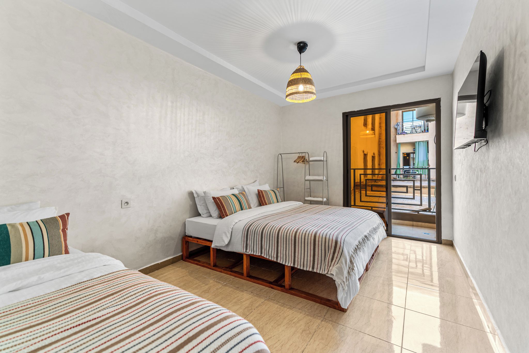 Quarto de hotel com cama, mesa de cabeceira, guarda-roupa, luminária pendente e vista para o exterior.