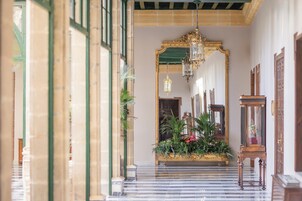 Um corredor imponente com um espelho grande e ornamentado, um lustre e uma mesa de madeira com um vaso.