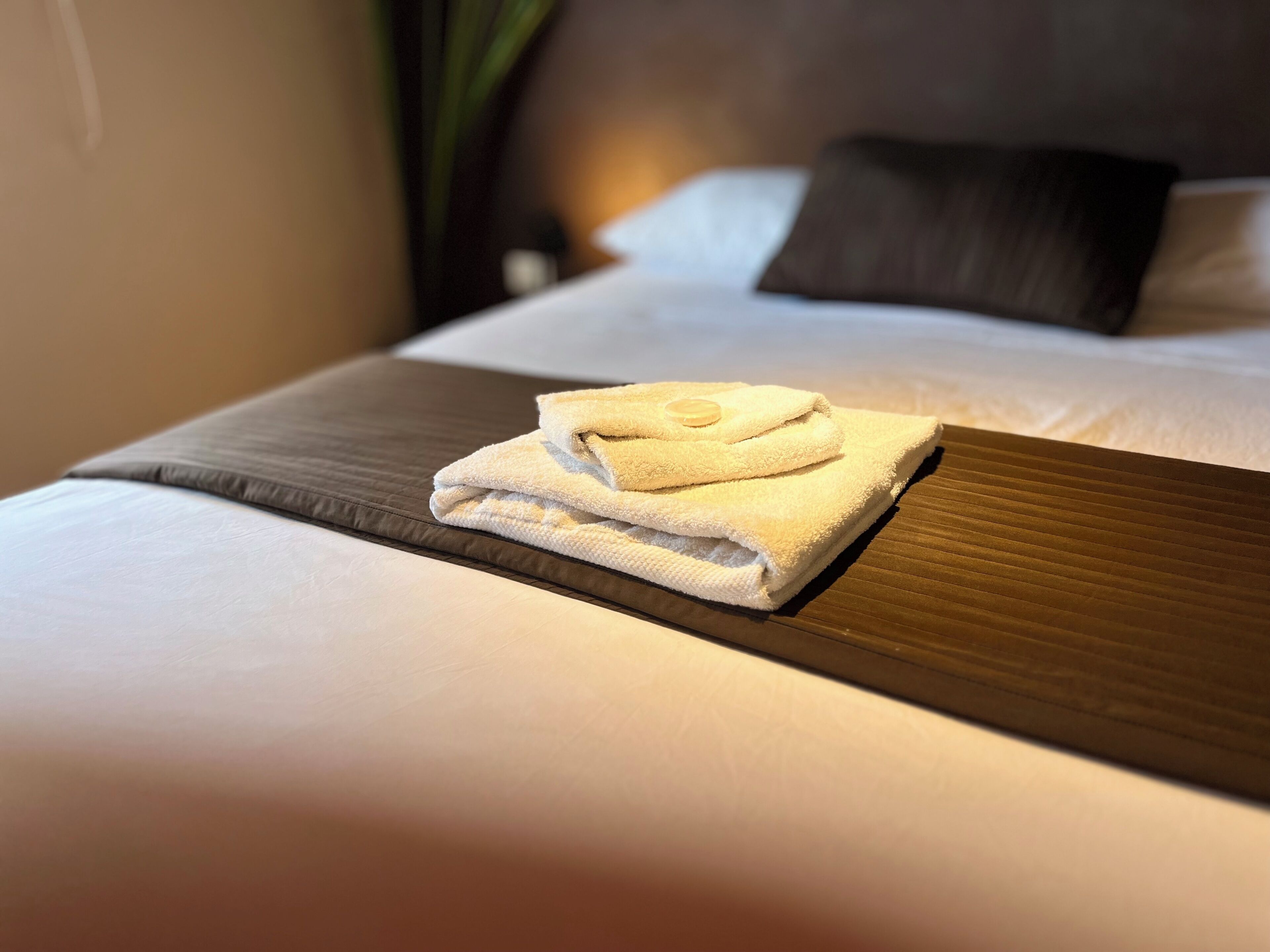 Cama bem arrumada com uma toalha dobrada e um tabuleiro de madeira.